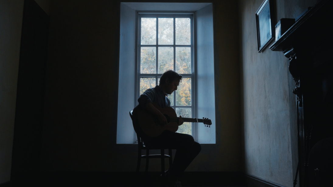 The silhouette of Joshua Burnside playing guitar beside a window in an ...